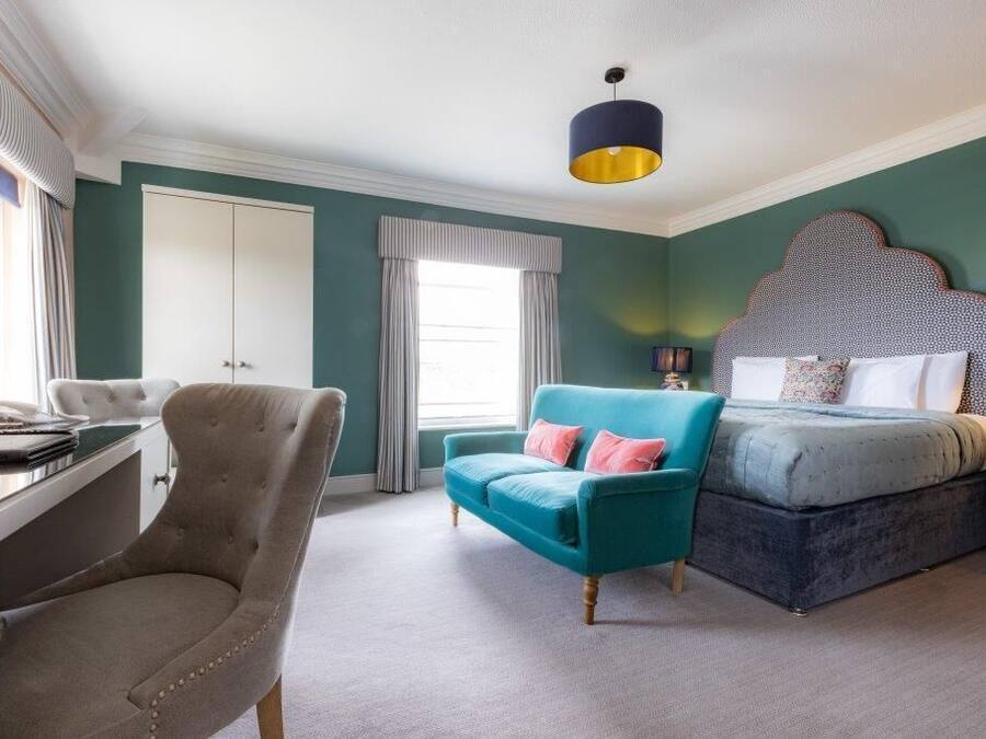 Quarto com parede verde-água, guarda-roupa branco, sofá verde-água, cama com cabeceira estampada e escrivaninha com cadeira.