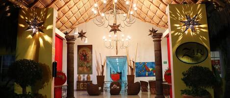 Um hall com teto de palha, um candelabro e plantas em vasos.
