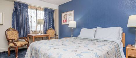 Quarto de hotel com uma cama grande, uma cadeira, uma escrivaninha e um abajur.