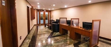 Corredor de hotel com piso de mármore, portas de madeira, balcão de recepção e área de estar.