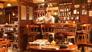 Um bar com móveis de madeira, um bartender e diversos frascos e copos nas prateleiras.