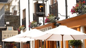 Uma área de estar externa com mesas de madeira e guarda-sóis brancos em um bar chamado "Carthy's Bar".