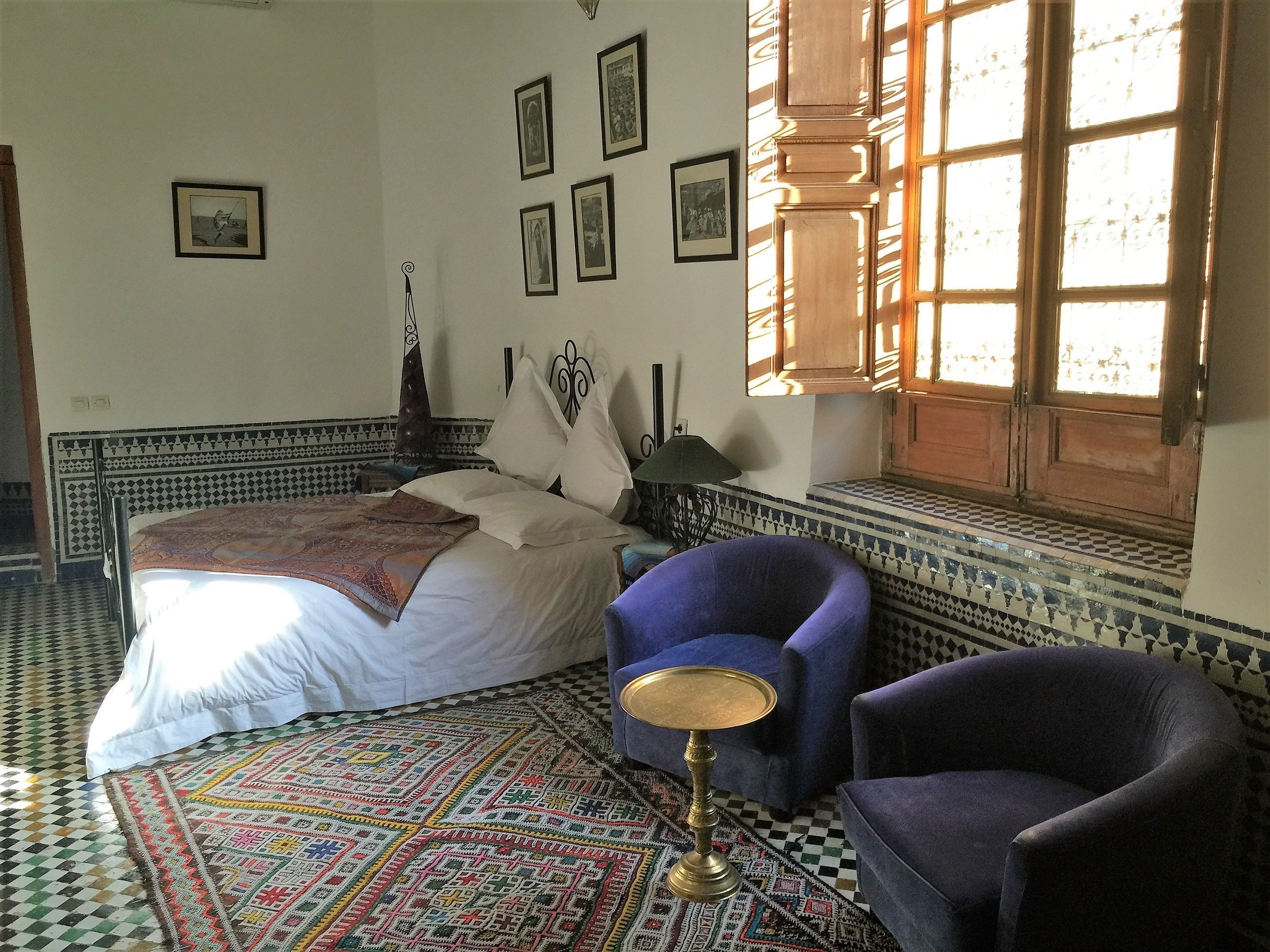 Um quarto com cama, poltrona, abajur e janela com cortinas estampadas.