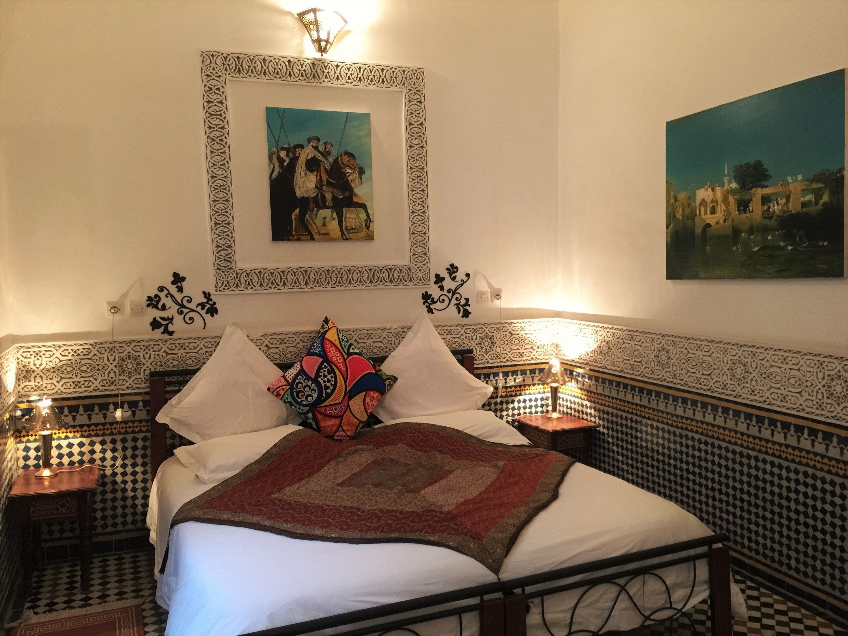 Quarto com cama, paredes estampadas, um quadro emoldurado e uma mesa de cabeceira com abajur.