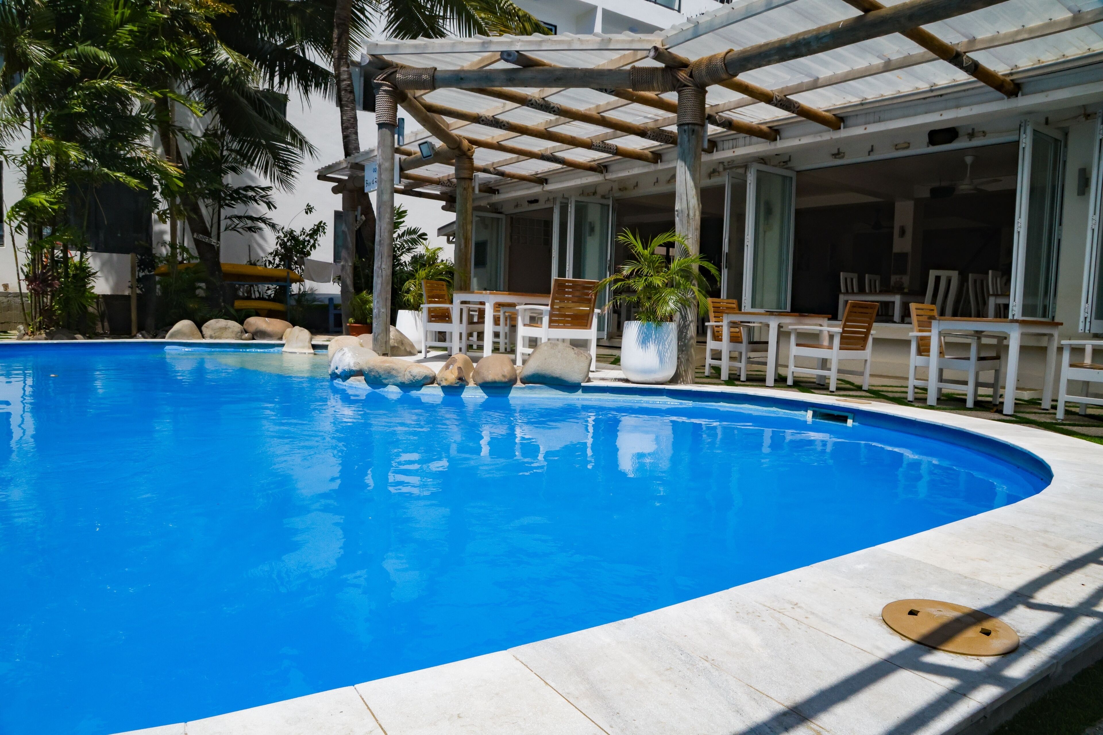 Uma área de piscina com pérgola, espreguiçadeiras e plantas em vasos.