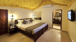 Quarto de hotel com cama, mesa de cabeceira, luminária e banheiro visível por uma porta aberta.