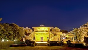 Edifício bem iluminado com vários níveis e varandas, cercado por vegetação.