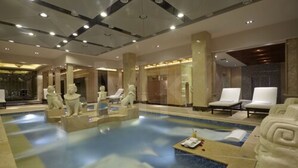 Uma grande piscina interior com estátuas, espreguiçadeiras e uma área de recepção.