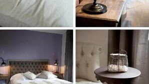 Quarto com cama, mesa de cabeceira, luminária, cadeira e pequena mesa com cesta.