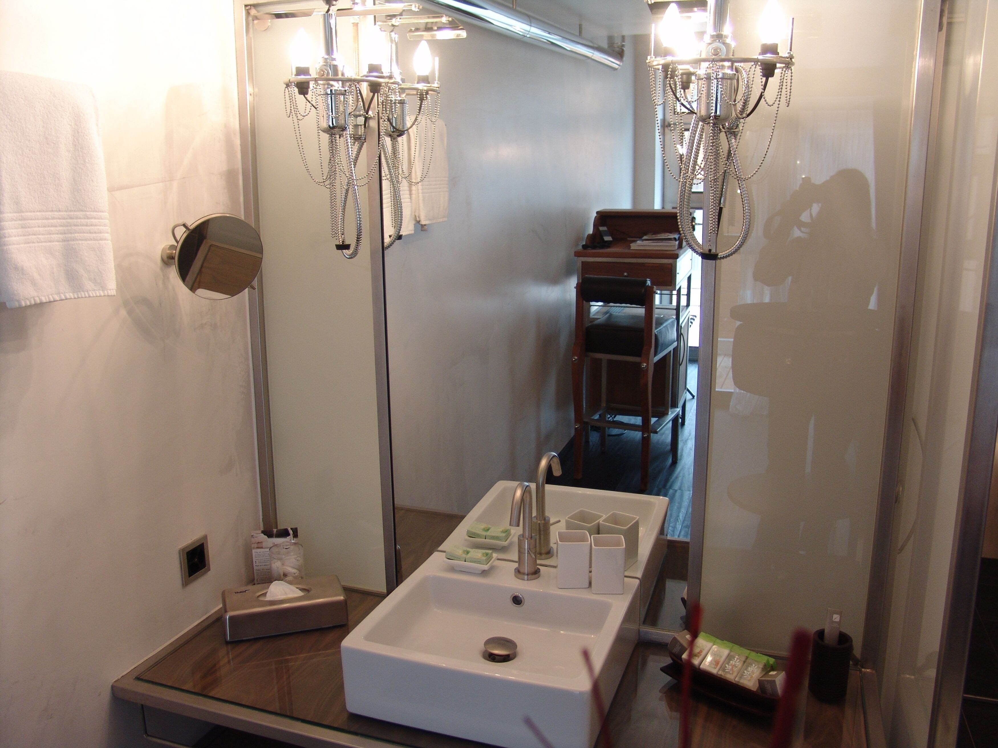 Casa de banho com lavatório branco, espelho, porta-toalhas e candelabro.