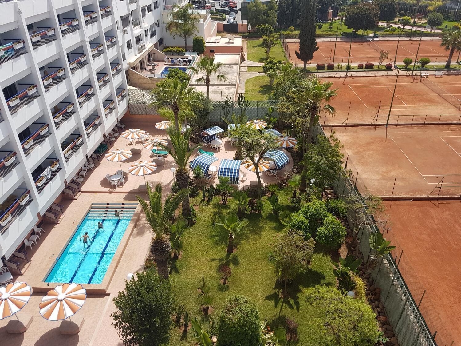 Um hotel com piscina, espreguiçadeiras e quadras de tênis.
