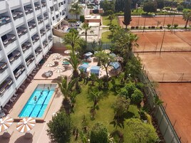 Um hotel com piscina, espreguiçadeiras e quadras de tênis.