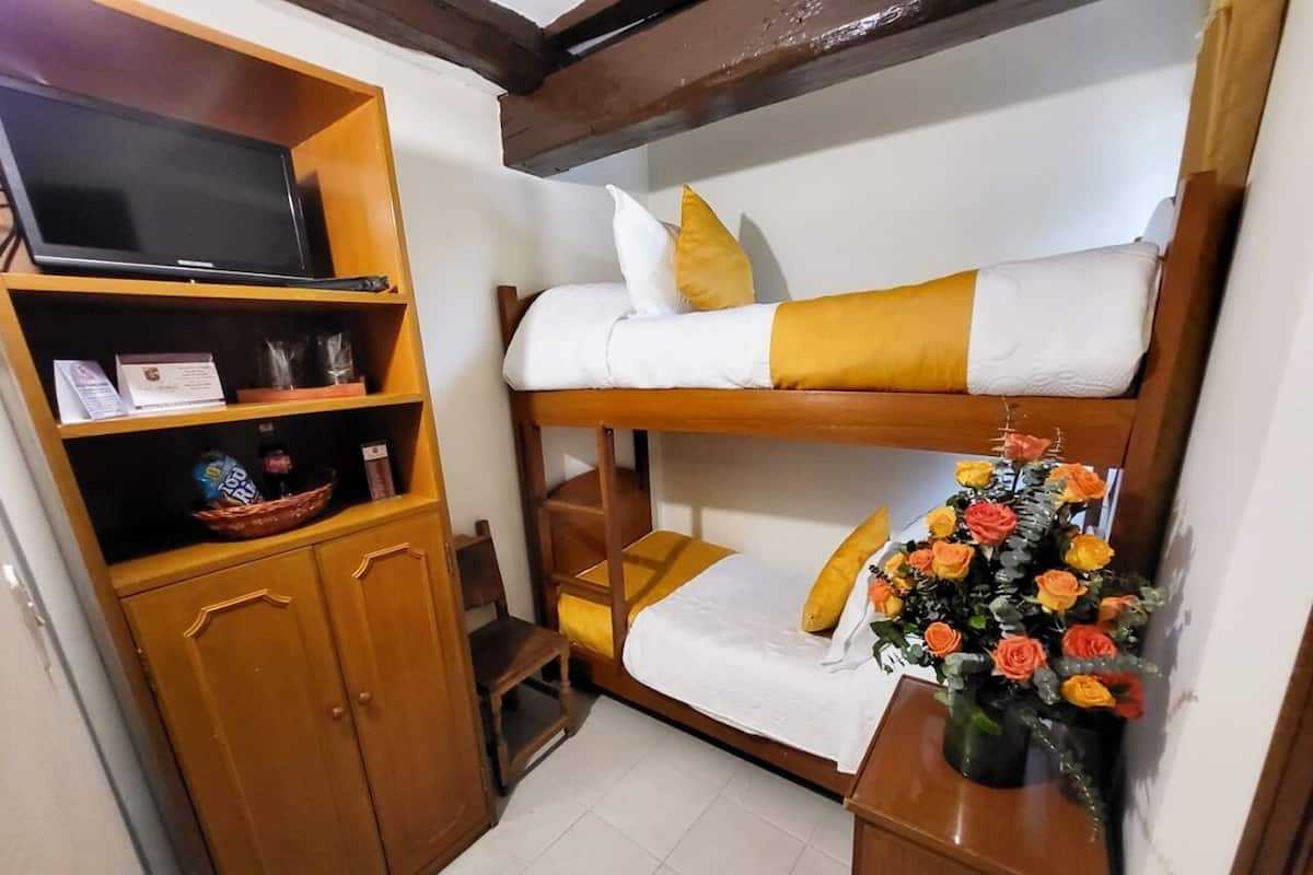 Quarto com beliche, guarda-roupa de madeira, uma mesinha e um vaso de flores.