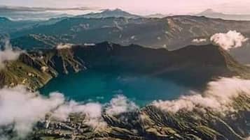 Vista aérea de uma cratera vulcânica, rodeada por campos verdes exuberantes e uma pequena aldeia.