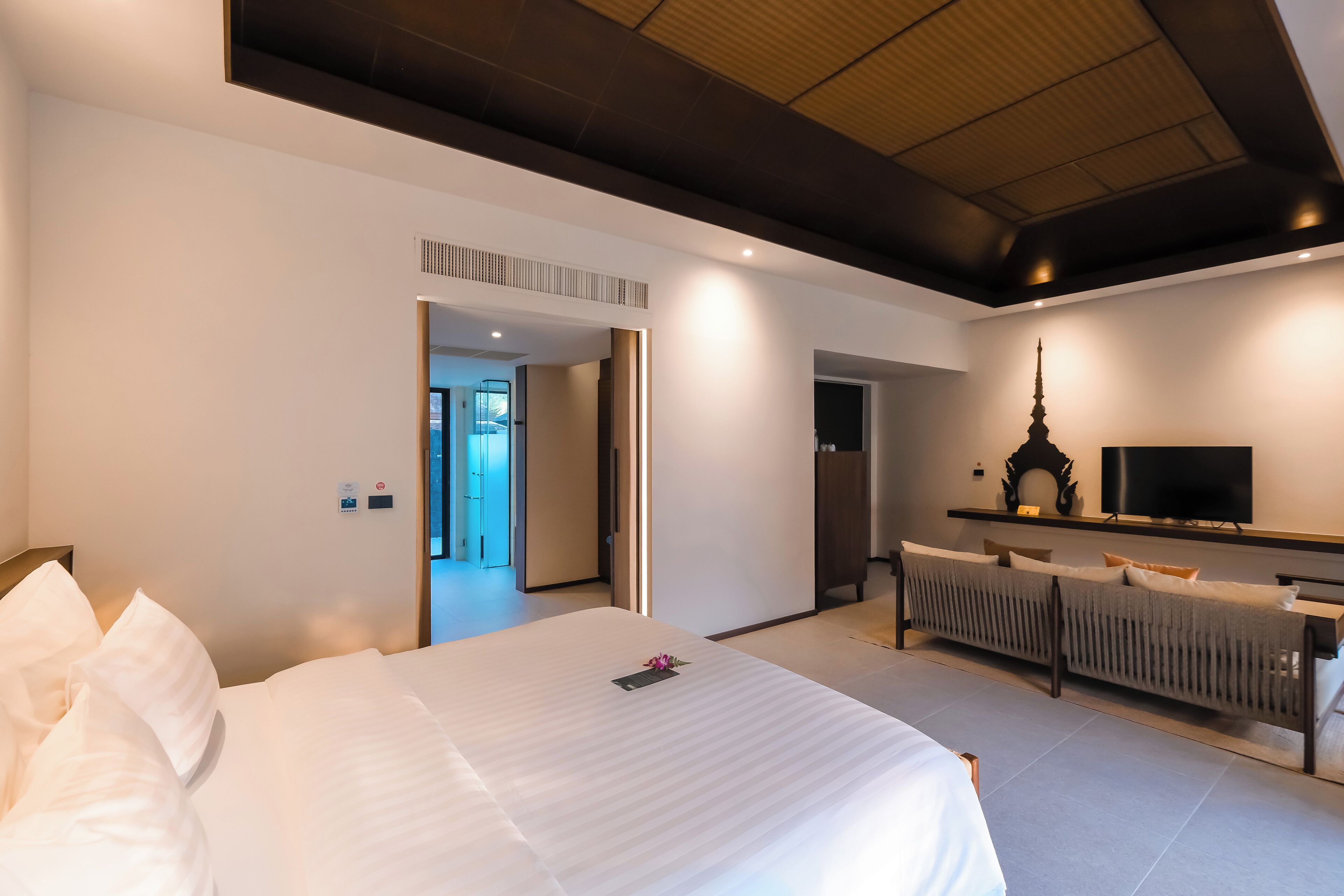 Quarto de hotel moderno com cama grande, sofá, televisão e um objeto decorativo na parede.