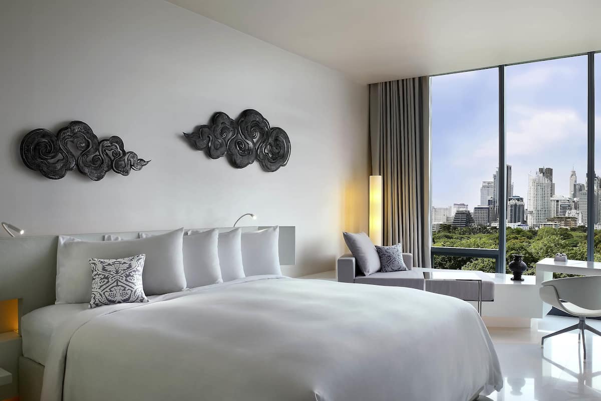 Quarto moderno com cama grande, escrivaninha e vista para a paisagem urbana.