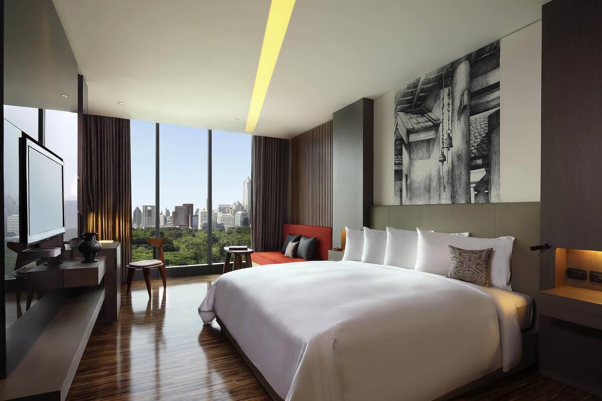 Quarto de hotel moderno com uma cama grande, televisão, escrivaninha e vista para a cidade.
