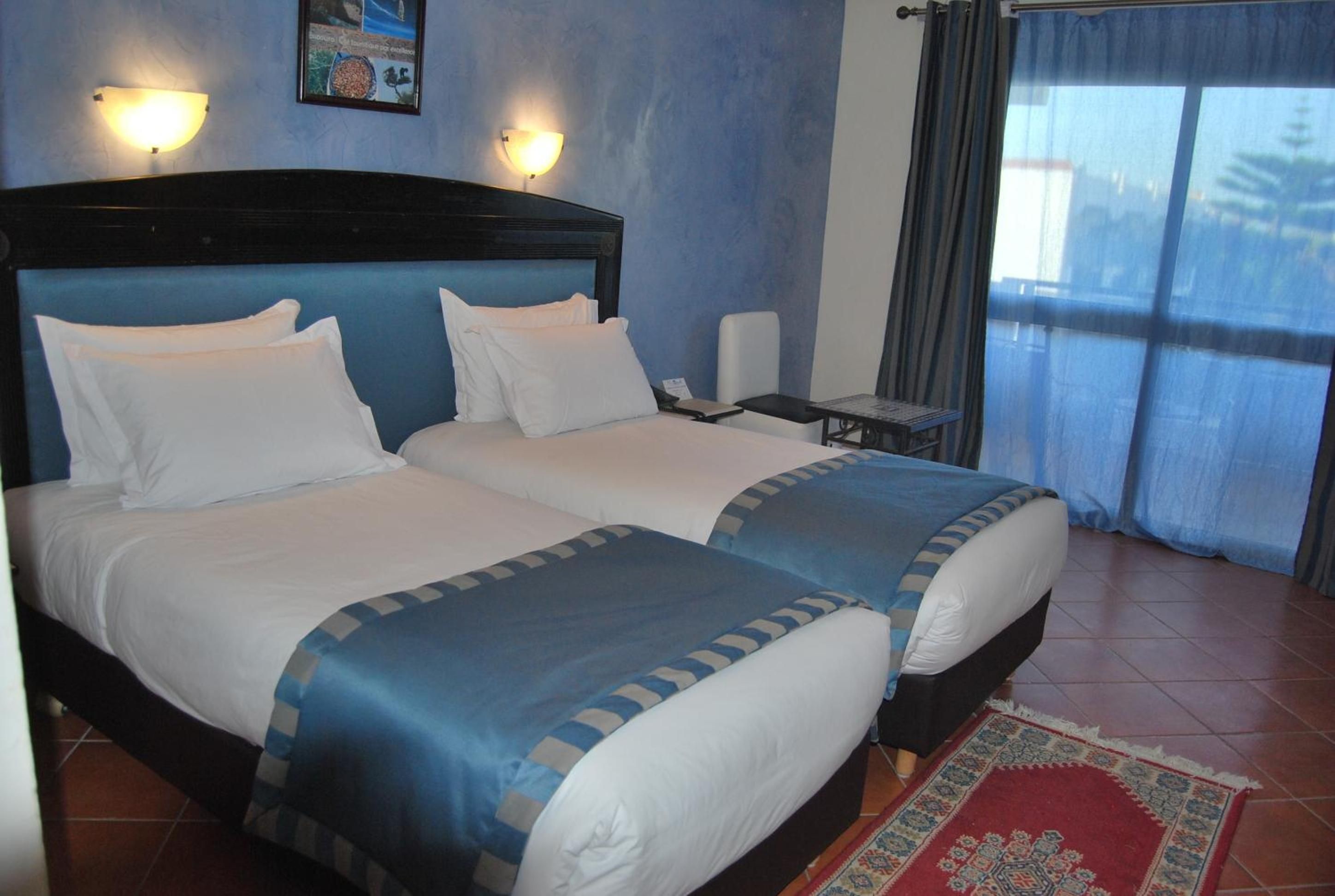 Uma cama de casal com cabeceira, duas mesas de cabeceira e uma janela com cortinas.