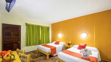 Quarto de hotel com duas camas, uma porta de madeira, cortinas verdes, uma pequena mesa com um vaso de flores e uma luminária na parede.