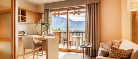Quarto de hotel moderno com cozinha, mesa de jantar, sofá e varanda com vista para as montanhas.