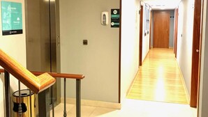 Um corredor de hotel com escada de madeira, elevador e área de recepção.