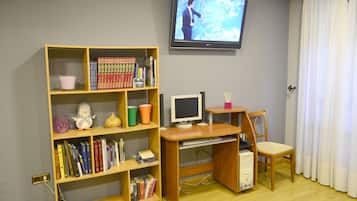 Um quarto com uma escrivaninha de madeira, um computador, uma estante de livros e uma televisão.