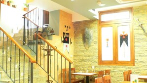 Interior de restaurante com escadaria, cadeiras de madeira, mesas e parede de pedra.