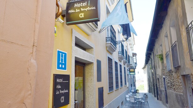 Uma rua estreita com placa de hotel, mesas ao ar livre e uma bandeira.