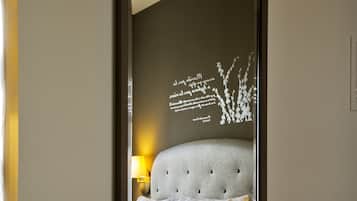 Quarto com cama, cadeira e espelho fixado na parede refletindo o ambiente.