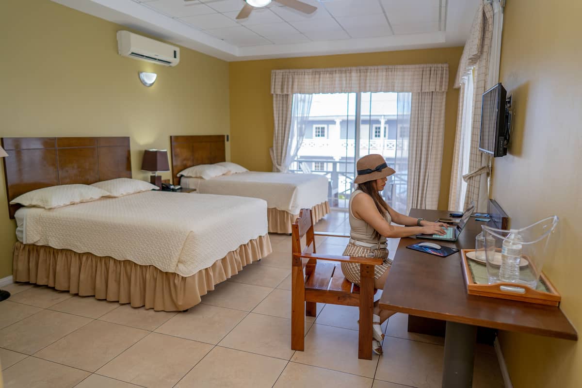 Quarto de hotel com duas camas, uma mesa de escritório com computador, televisão e janela com cortinas.