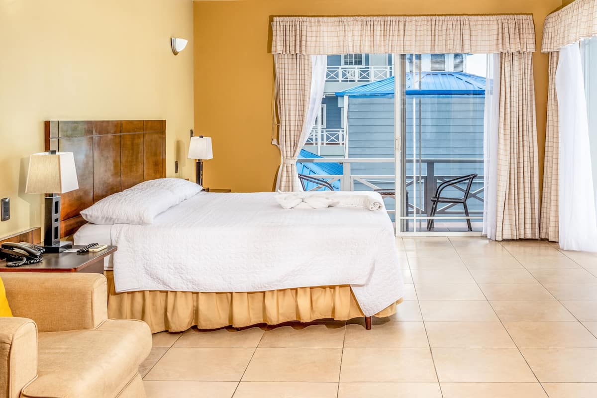Quarto de hotel com cama, poltrona, escrivaninha com luminária e varanda com cadeira.