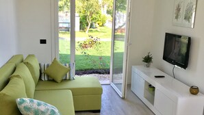 Uma sala de estar moderna com um sofá verde, um suporte de TV branco e uma porta de vidro deslizante que dá para um jardim.