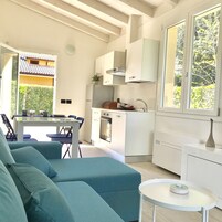 Cozinha moderna com armários brancos, área de refeições com cadeiras azuis e uma grande janela com vista para o verde.