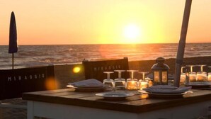 Mesa posta para dois com vista para o pôr do sol sobre o oceano.