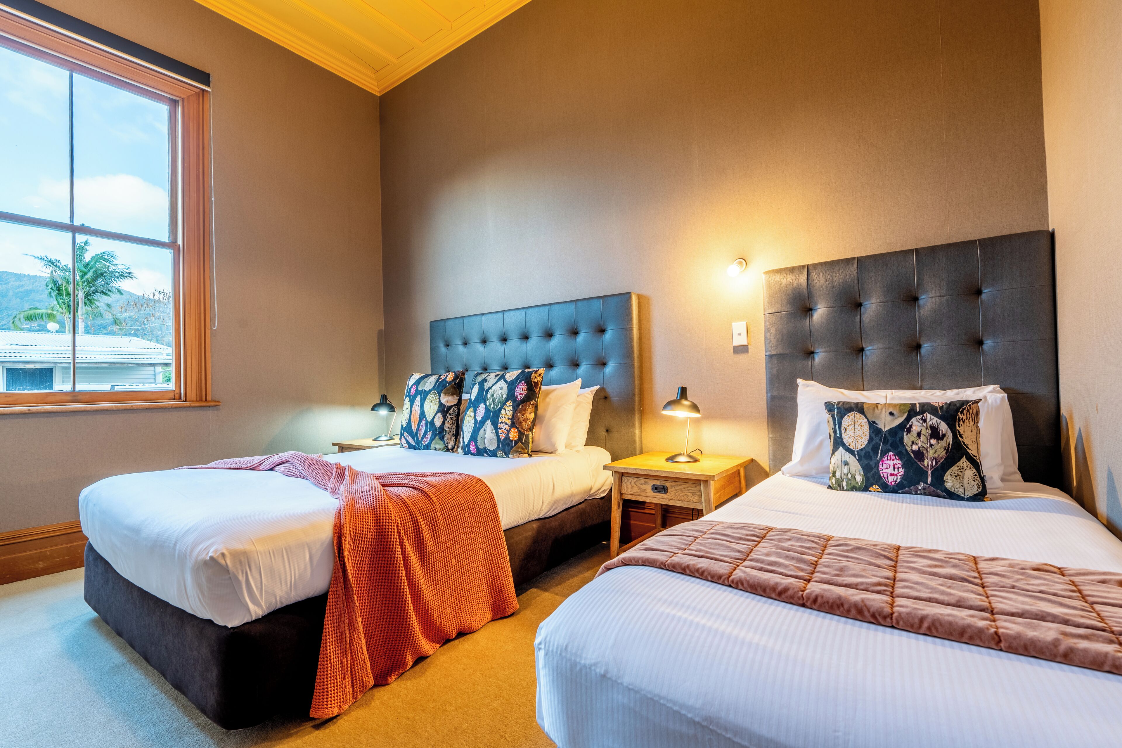 Quarto de hotel com duas camas, uma janela grande e vista para palmeiras.