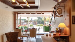 Um saguão de hotel com uma mesa de recepção de madeira, duas poltronas estofadas, uma poltrona estampada, um relógio e um abajur.