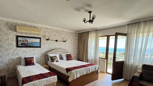 Quarto de hotel com duas camas, um ventilador de teto, um lustre, vista para o mar e uma varanda.