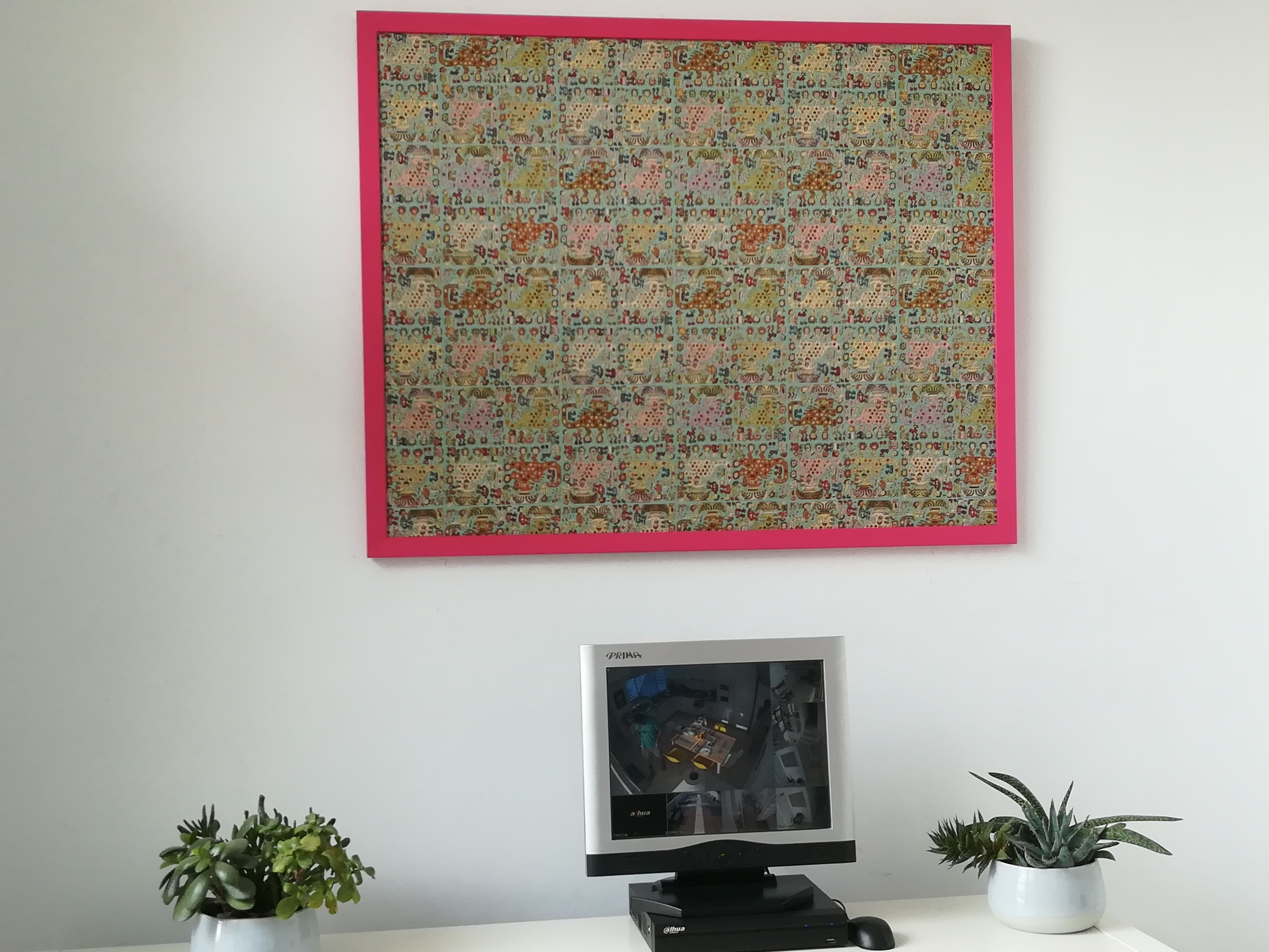 Quarto com televisão de tela plana em um suporte, duas plantas em vasos e uma obra de arte abstrata colorida na parede.