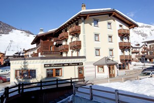 Um edifício com várias andares, varandas, um letreiro de restaurante e uma montanha nevada ao fundo.