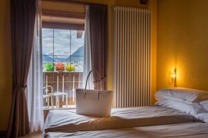 Quarto de hotel com uma cama, vista para montanhas e janela com cortinas.