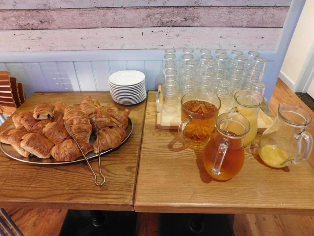 Disposição para o café da manhã com pães e bebidas sobre uma mesa de madeira.