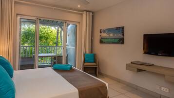 Quarto de hotel com cama, cadeira, televisão e varanda com vista para área verde.