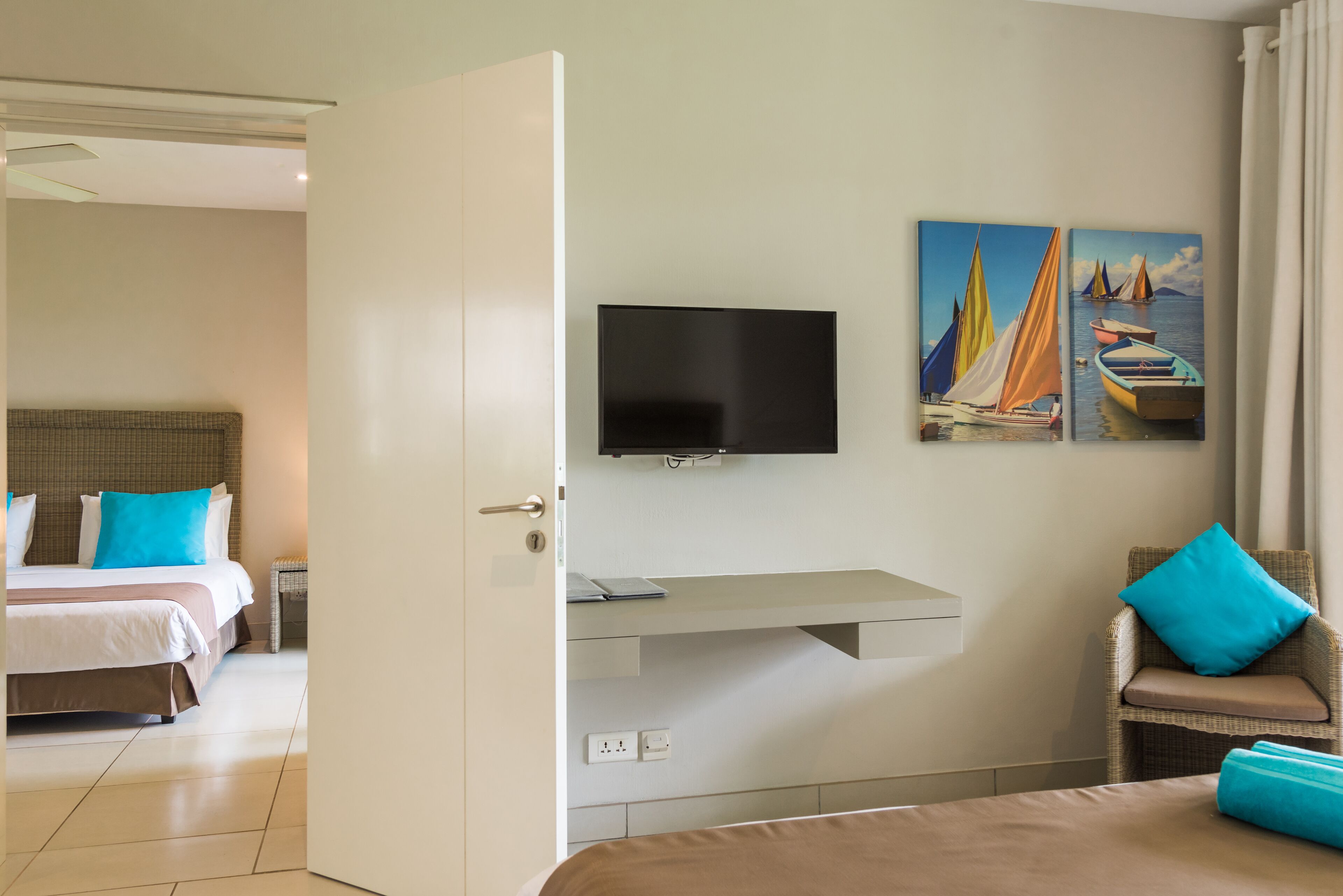 Quarto de hotel com uma cama, uma televisão na parede, uma cadeira com almofada e um quadro de veleiros.