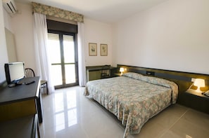 Quarto de hotel com cama, escrivaninha, cadeira e janela com cortinas.