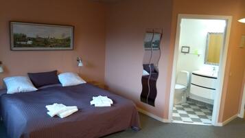 Quarto de hotel com uma cama grande, um quadro na parede, um espelho e um banheiro visível através de uma porta aberta.