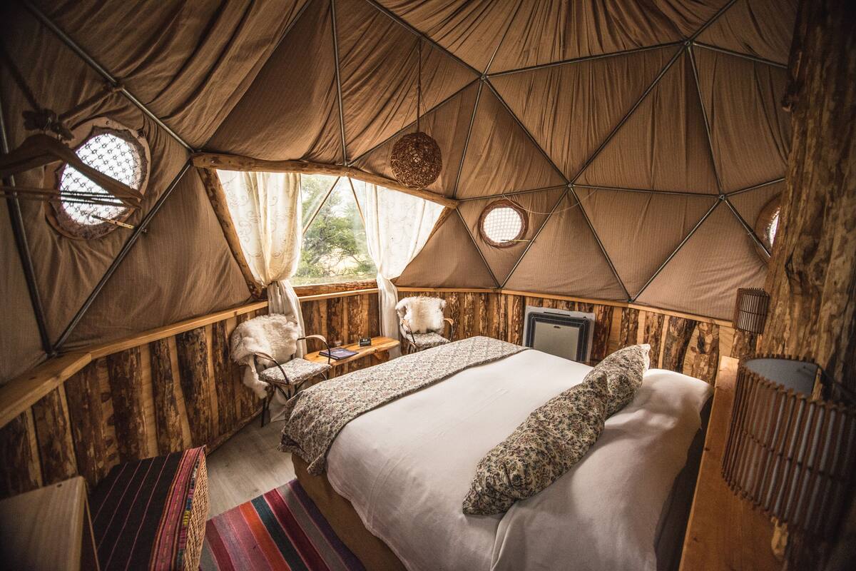 Uma tenda acolhedora com uma cama, uma cadeira, uma mesa e uma pequena janela.