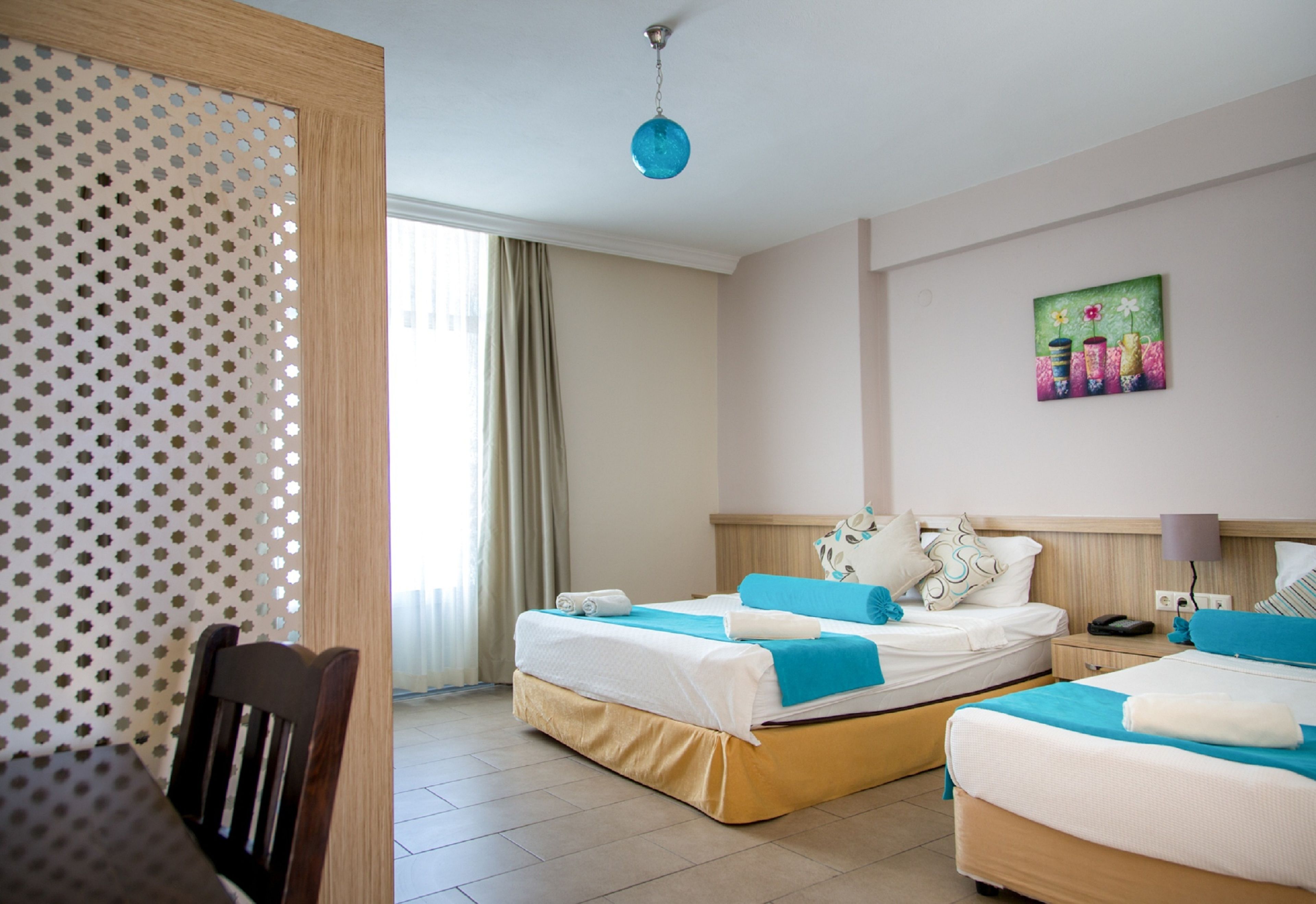 Quarto de hotel com duas camas, cabeceira de madeira, mesa de jantar e um elemento decorativo na parede.