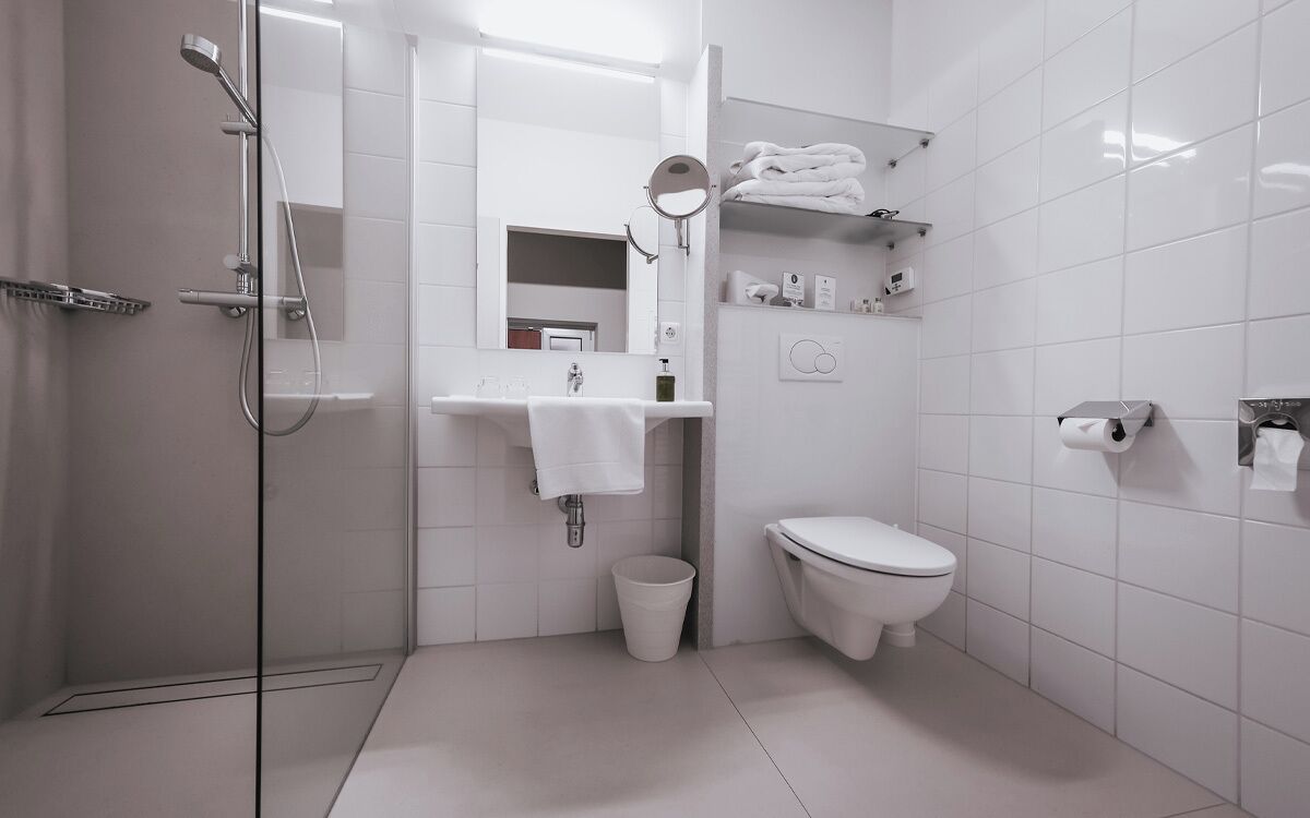 Uma casa de banho moderna com chuveiro, sanita, lavatório e espelho.