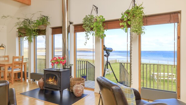 Uma sala de estar aconchegante com lareira, sofá de couro e amplas janelas com vista para uma praia.