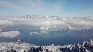 Vista panorâmica de uma paisagem montanhosa coberta de neve, com um lago, teleférico e área arborizada.